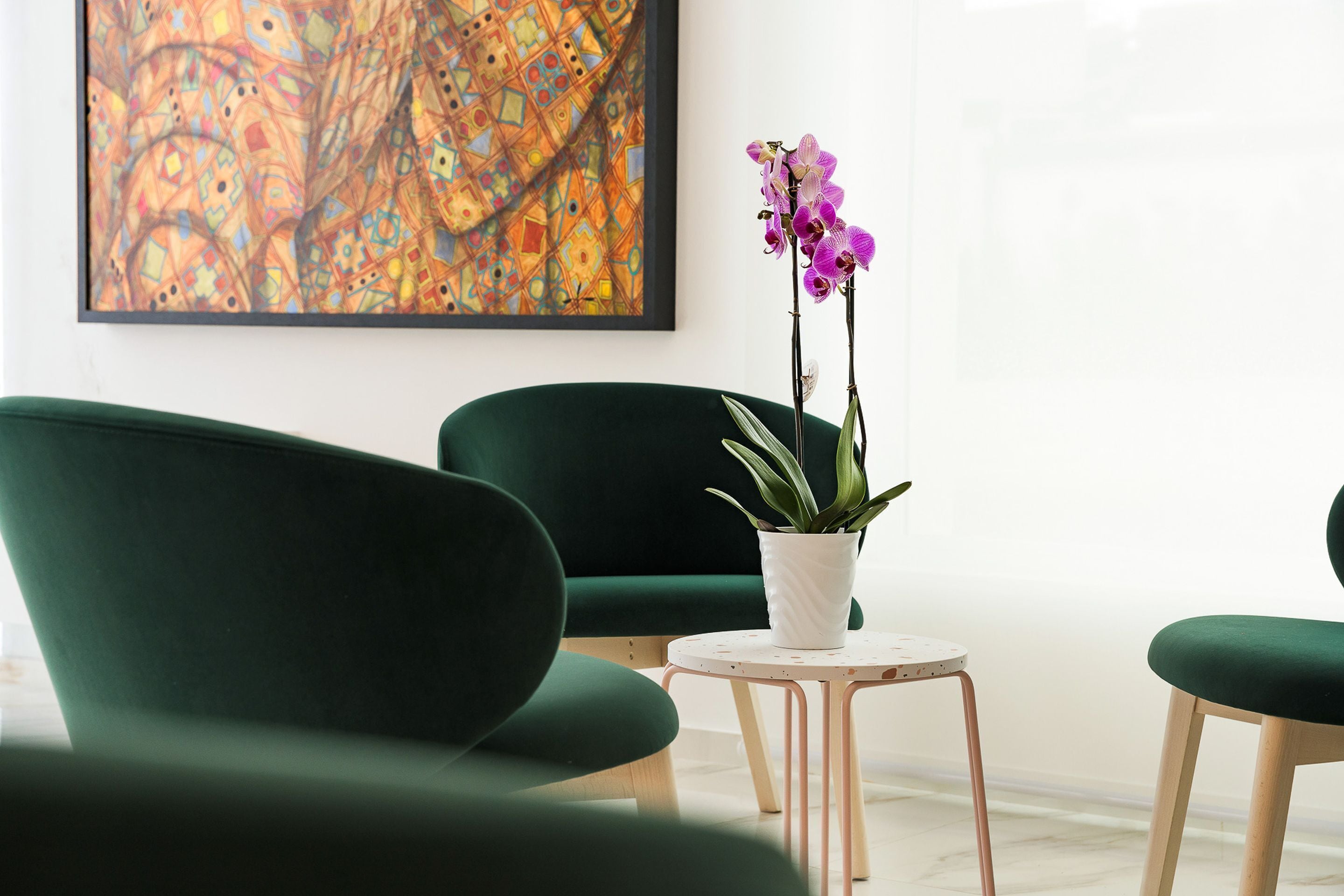Quarto com um sofá verde, uma mesa pequena branca e uma orquídea em vaso.