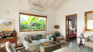 Uma sala de estar aconchegante com sofá, poltronas, mesa de centro e uma janela grande com vista para o verde.