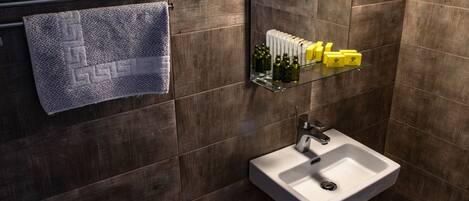 Um banheiro com pia branca, azulejos marrons escuros, um porta-toalhas com toalha estampada e uma prateleira com produtos de higiene pessoal.