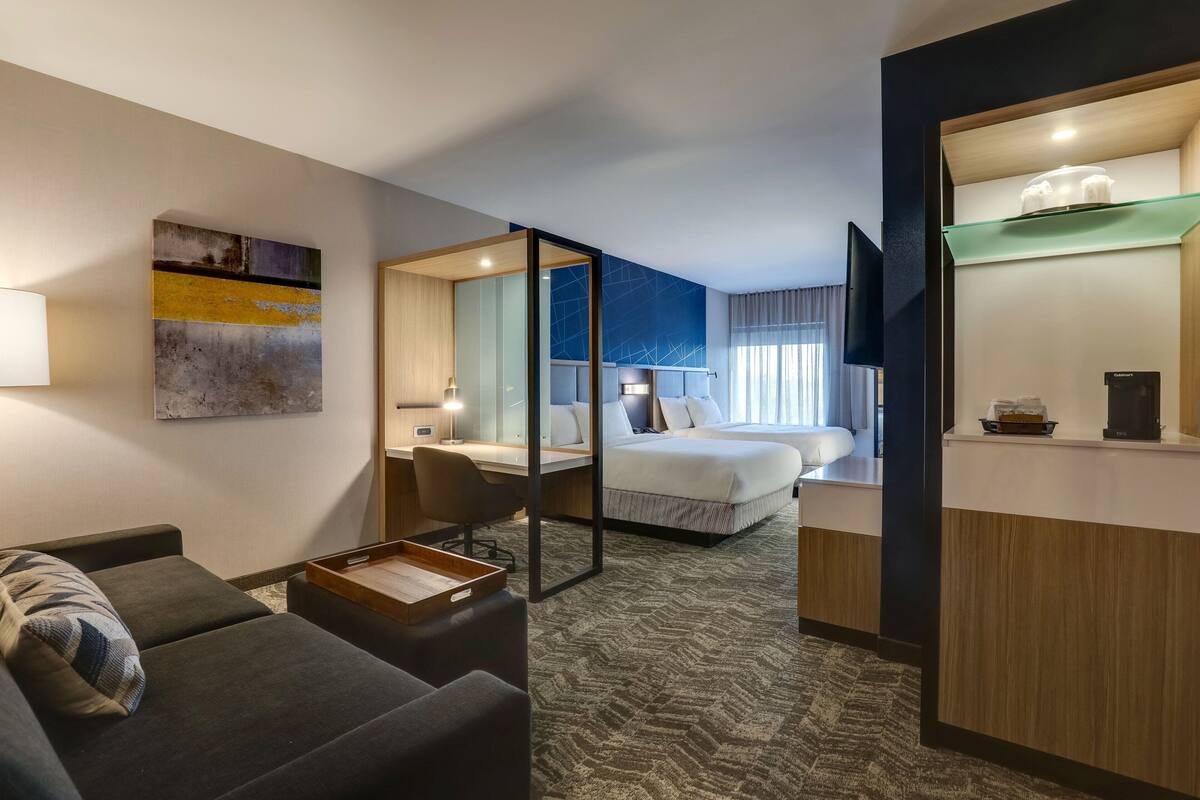 Quarto de hotel com cama, escrivaninha, cadeira, sofá e um quadro na parede.