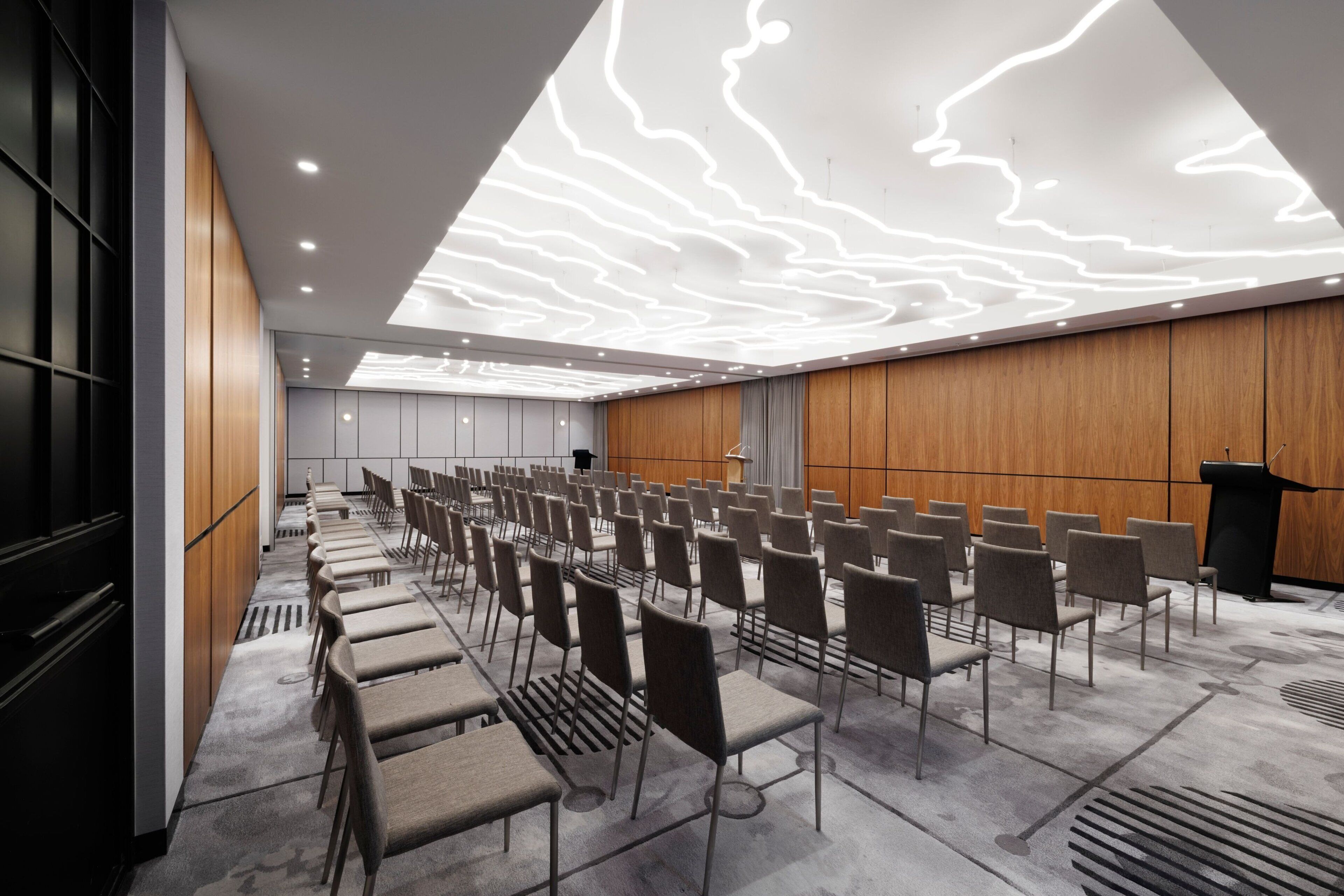 Sala de conferências com fileiras de cadeiras, um pódio e um design moderno no teto.