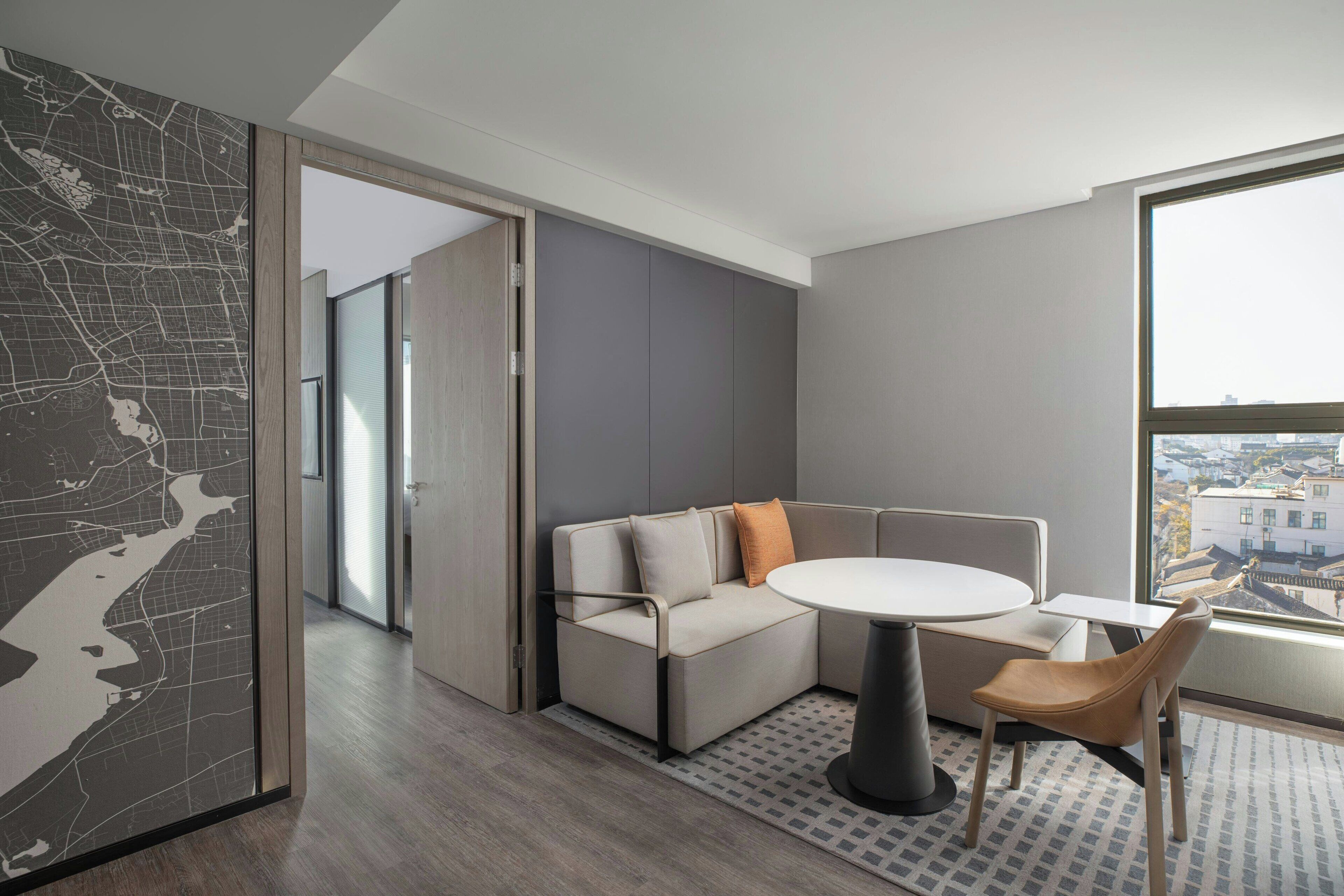 Uma sala de estar moderna com um sofá seccional, uma mesa redonda e vista da cidade através de grandes janelas.