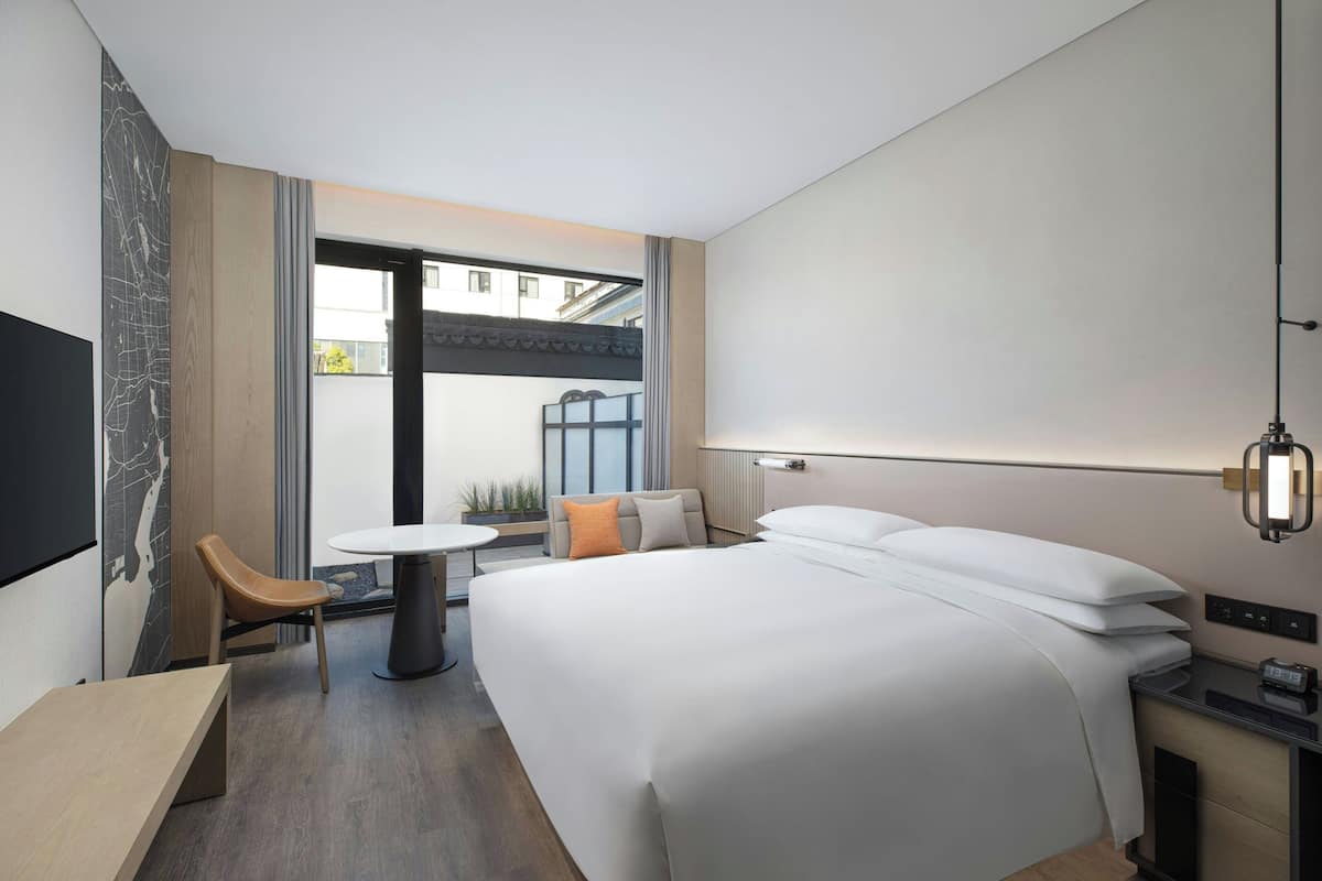 Quarto de hotel moderno com uma cama grande, uma escrivaninha, uma cadeira e uma mesinha.