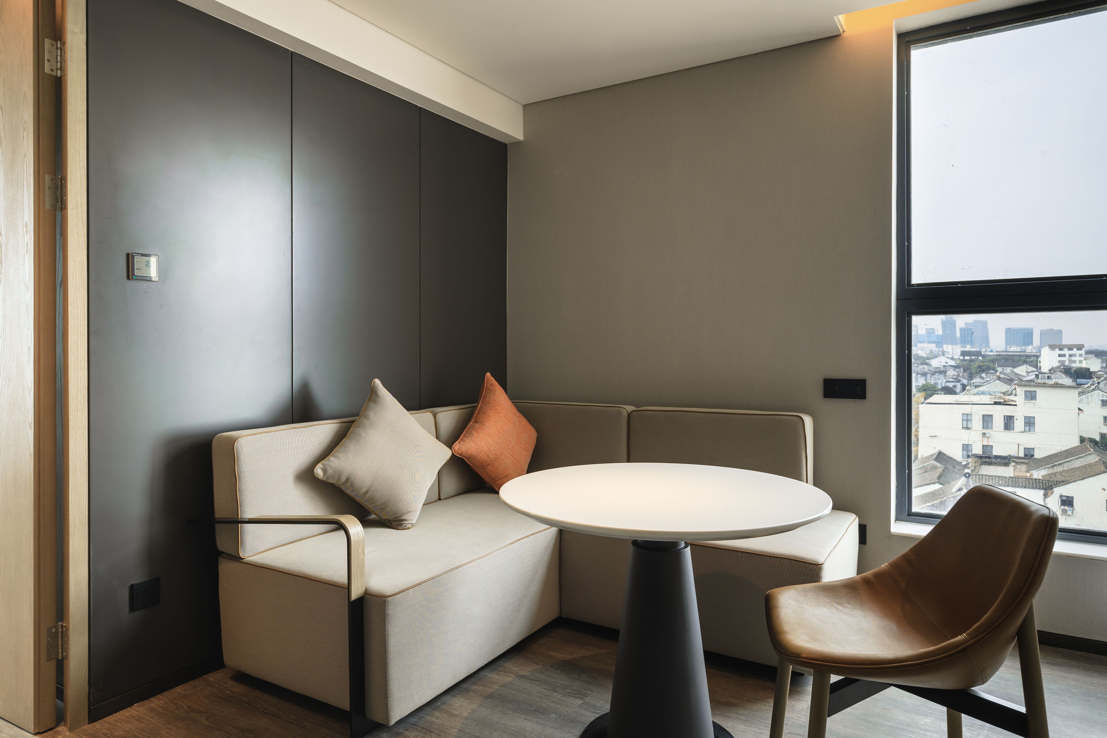 Quarto moderno com sofá, mesa redonda, janela com vista para a cidade e uma porta.