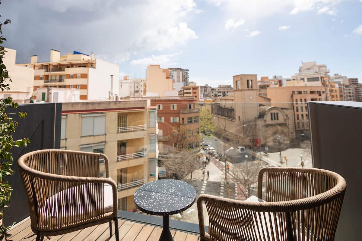 Uma varanda com cadeiras de vime e uma pequena mesa, com vista para um horizonte urbano com diversos edifícios.