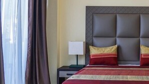Quarto de hotel com uma cama grande, uma mesa de cabeceira, um abajur e um aparelho de ar condicionado na parede.