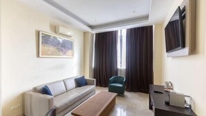 Uma sala de estar moderna com sofá, mesa de centro, poltrona, TV na parede e janela com cortinas.