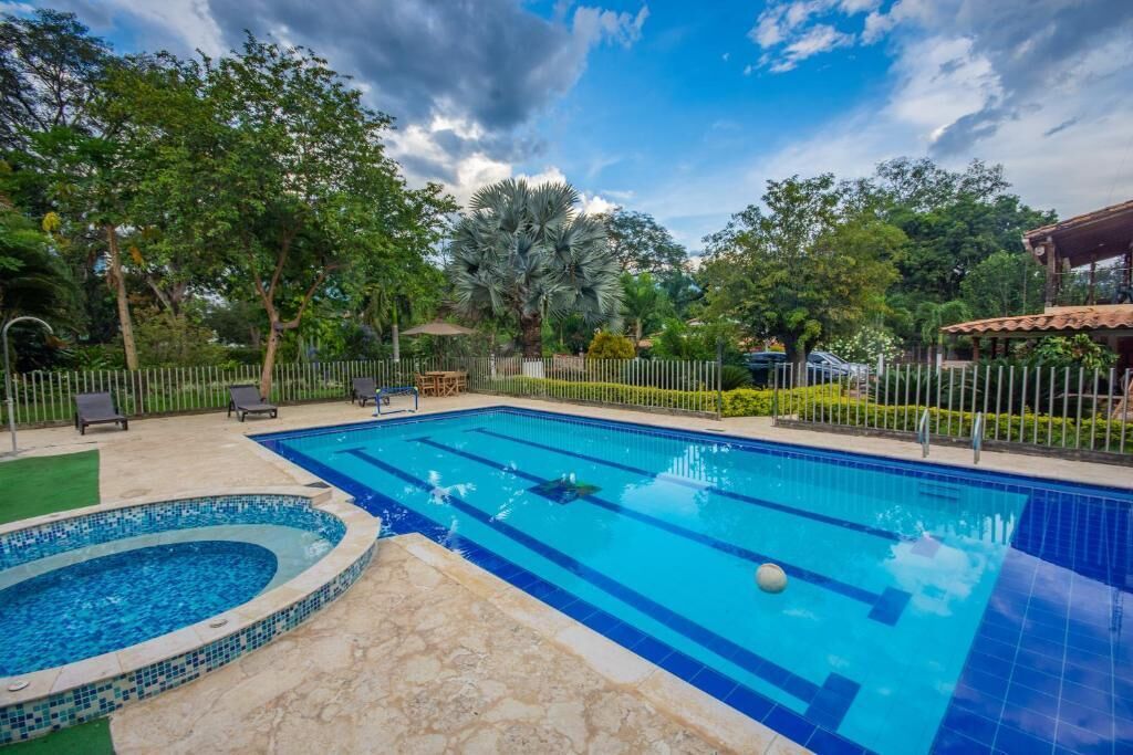 Piscina com deck ladrilhado, cercada por uma vedação e árvores.