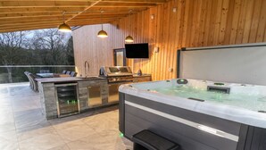 Uma área de cozinha externa com hidromassagem, churrasqueira e espaço de estar com cadeiras e mesa.