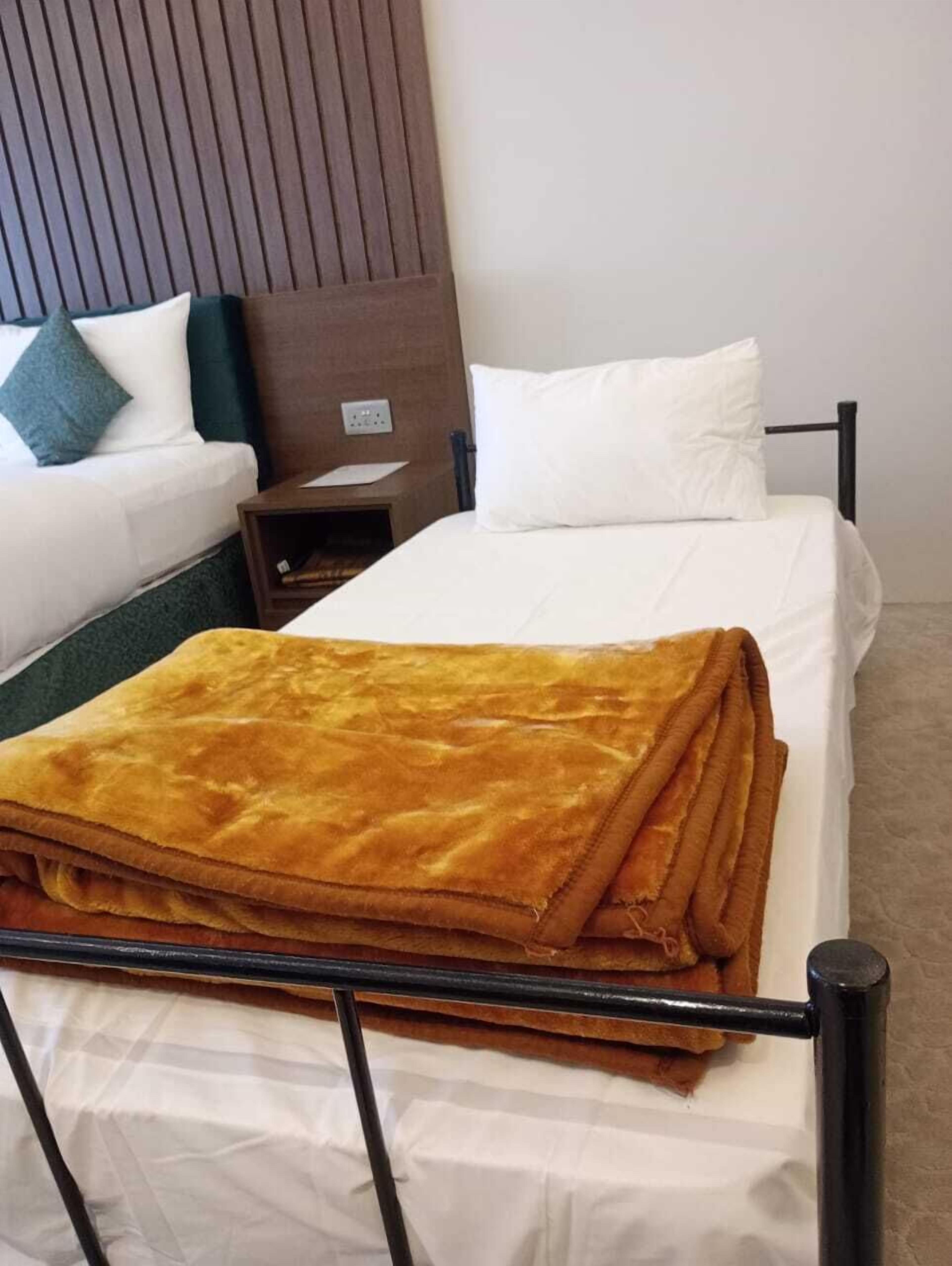 Quarto de hotel com uma cama, uma mesinha de cabeceira e um cobertor dobrado na cama.