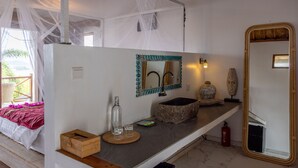 Quarto com cama, banheiro com pia e espelho, um banco de madeira e um extintor de incêndio.