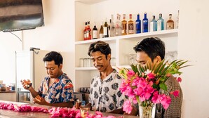 Uma área de bar com teto de madeira, balcão adornado com guirlanda de flores e prateleiras com garrafas.