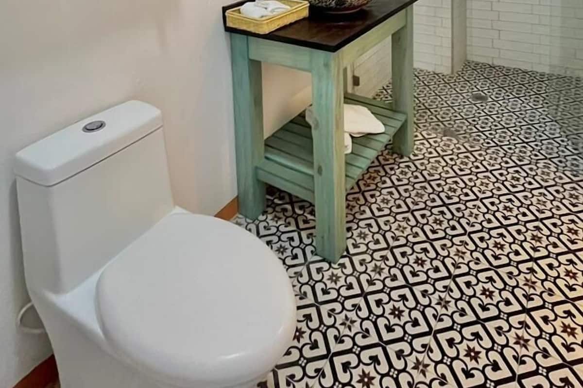 Casa de banho com sanita, lavatório com uma tigela decorativa, cabine de duche em vidro e azulejos com padrão.