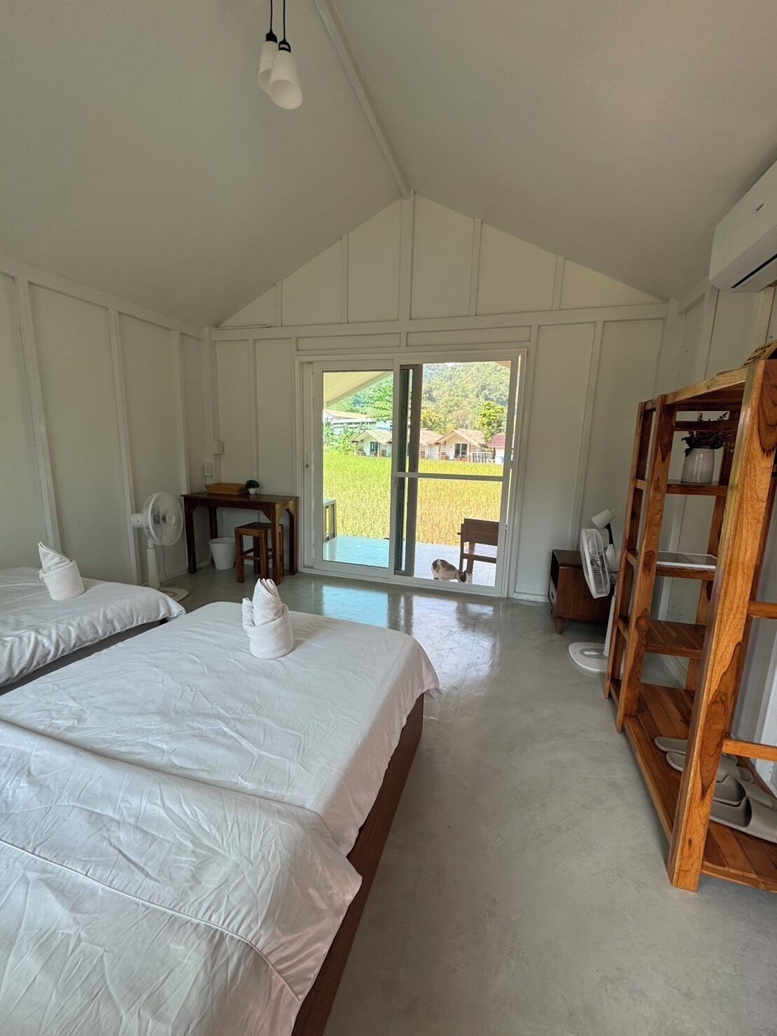 Quarto de hotel com duas camas, um guarda-roupa de madeira, uma secretária e vista para uma paisagem verde através das portas de correr.