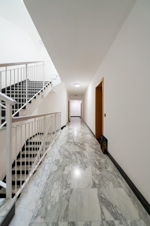Um corredor com piso de mármore, corrimão branco e uma porta de madeira no final.