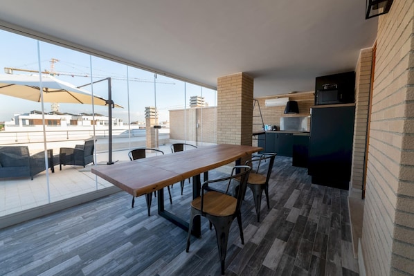 Uma cozinha moderna com uma janela grande, uma área de jantar com mesa e cadeiras de madeira, e vista para o horizonte da cidade.