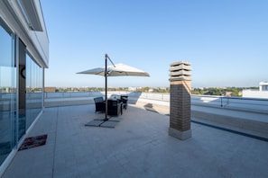 Terraço no telhado com mesa e cadeiras, um guarda-sol grande e um pilar decorativo.
