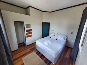 Quarto com cama, uma pequena mesa de trabalho, porta e piso de madeira.