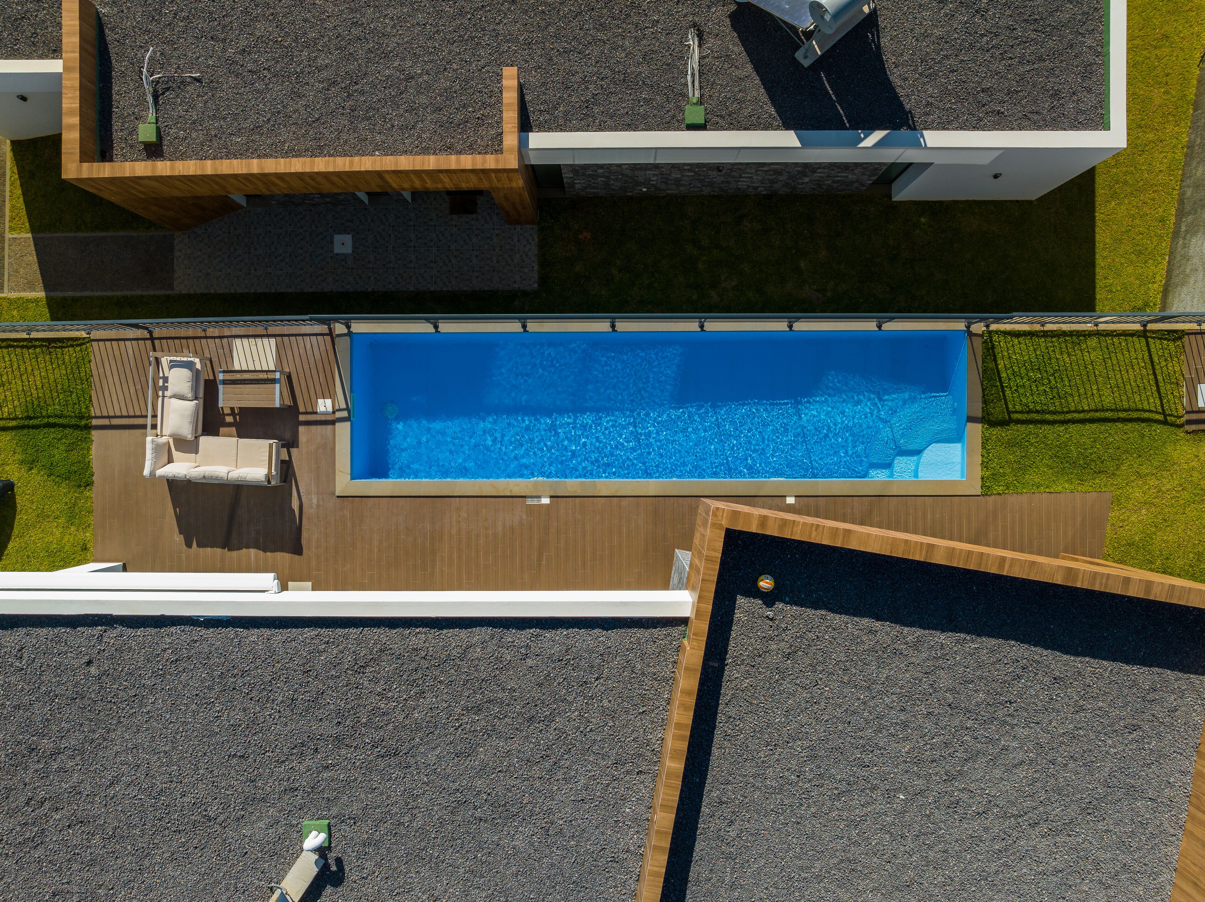 Piscina moderna ao ar livre com deck de madeira, espreguiçadeiras e pérgola.