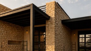 Uma casa moderna com paredes de pedra, alpendre coberto e gramado bem cuidado.