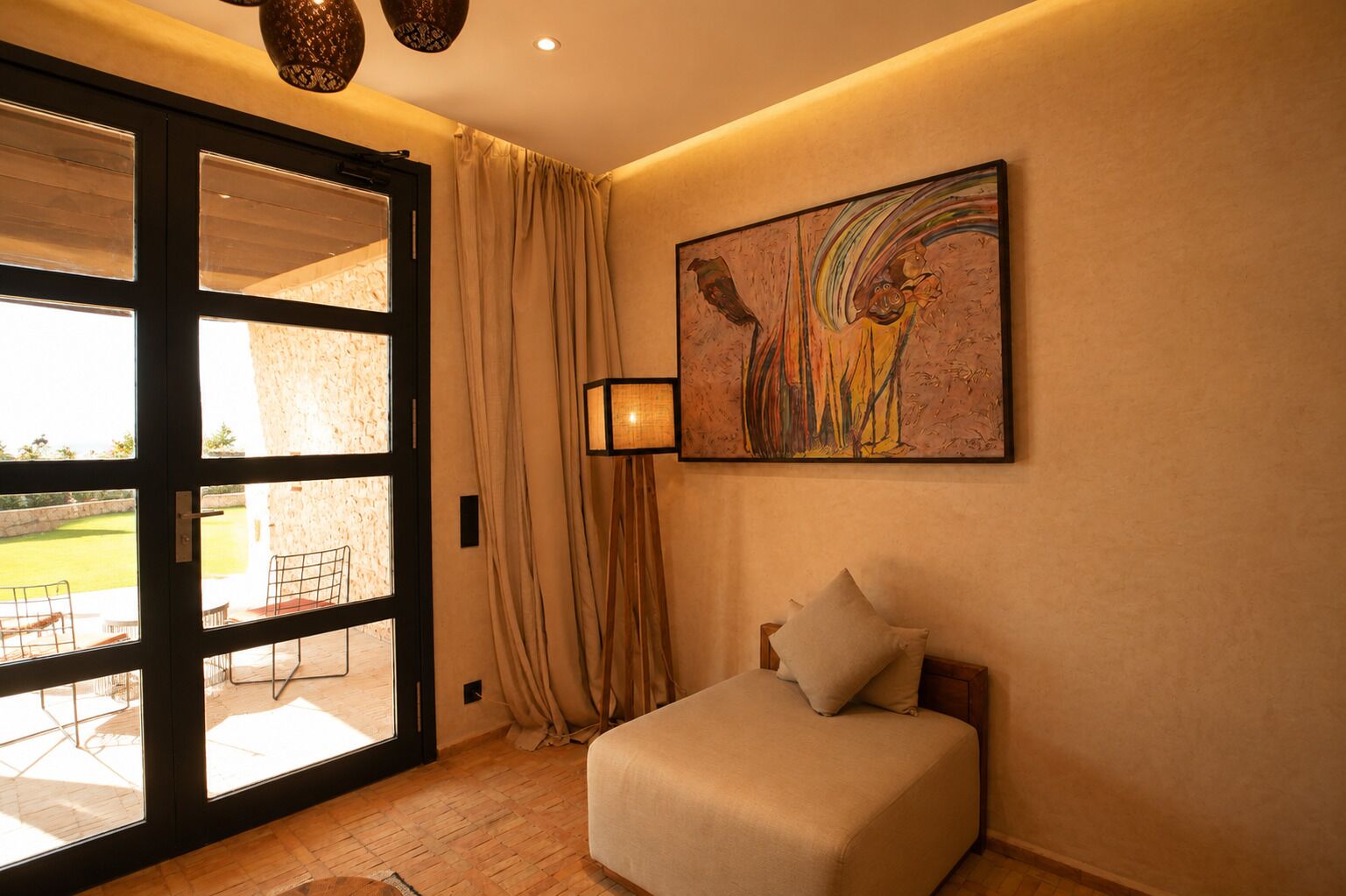 Quarto com uma cama, um quadro, uma luminária e vista através de uma porta de vidro.