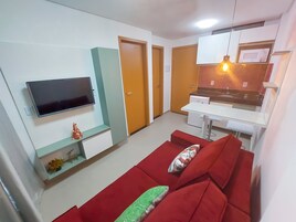 Um espaço de estar compacto com televisão de tela plana, cozinha compacta, sofá vermelho e mesa de jantar.