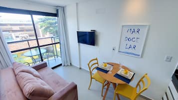 Quarto moderno com sofá, mesa de jantar com cadeiras, TV na parede e varanda com mobiliário para área externa.