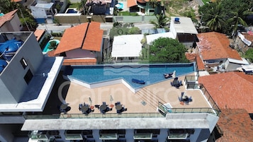 Piscina no terraço com espreguiçadeiras e guarda-corpo de vidro.