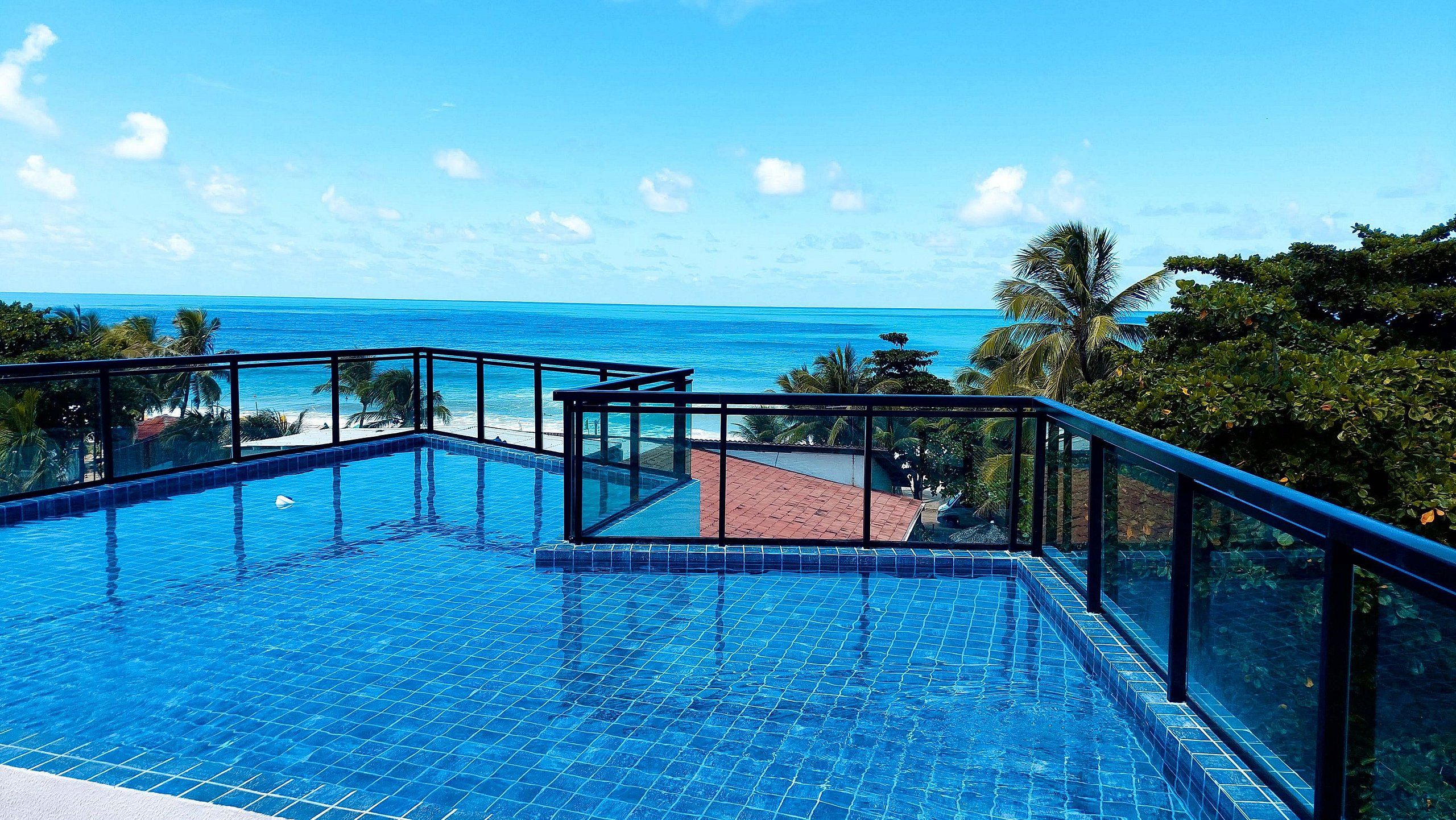 Uma piscina infinita azul cristalina com barreira de vidro, com vista para uma praia e oceano.