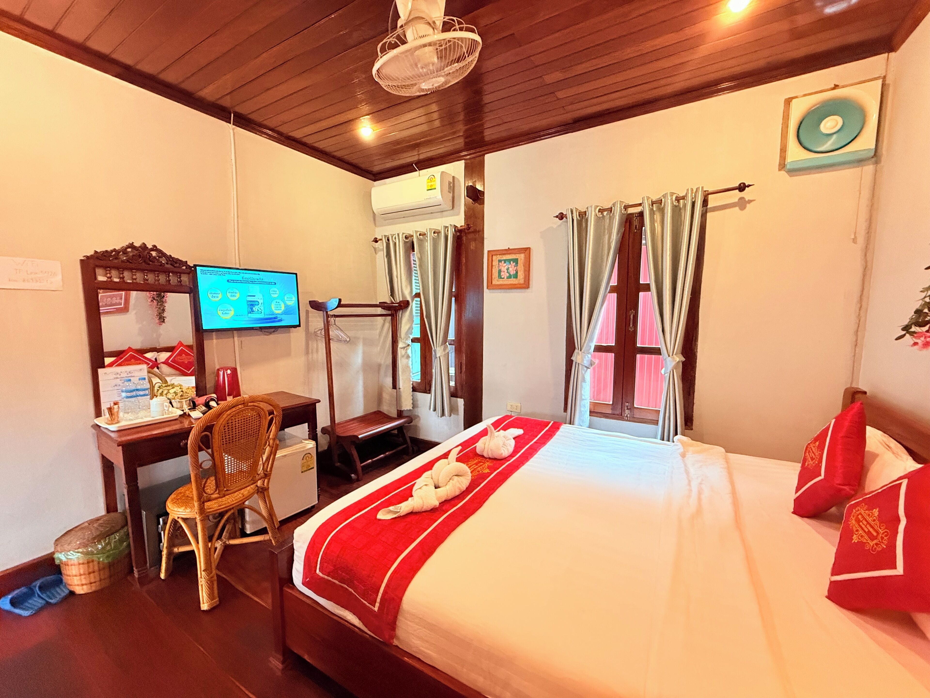 Quarto de hotel com cama, escrivaninha com computador, cadeira, televisão e janela com cortinas.