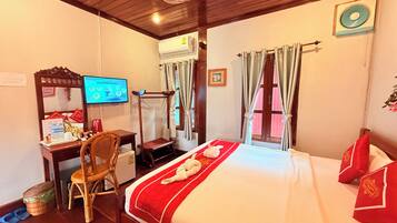 Quarto de hotel com cama, escrivaninha com computador, cadeira, televisão e janela com cortinas.