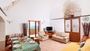 Uma sala de jantar com uma mesa posta para quatro pessoas, um sofá e uma televisão.