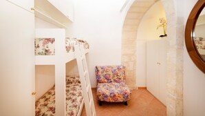 Um quarto com beliches, uma poltrona estampada com flores e um arco de pedra.