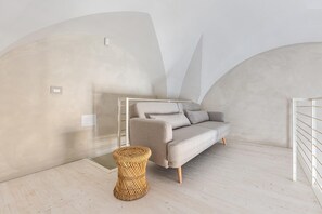 Quarto moderno e minimalista com um sofá cinzento, um banquinho trançado e um corrimão branco.