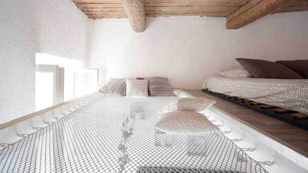 Quarto com teto alto, cama com roupa de cama estampada, um pequeno sofá e piso de malha branca.