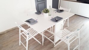 Uma mesa de jantar branca com quatro cadeiras, uma garrafa de água, um copo e uma pequena planta.