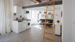 Uma cozinha moderna com eletrodomésticos brancos, uma escada de madeira e uma área de jantar com um sofá listrado.