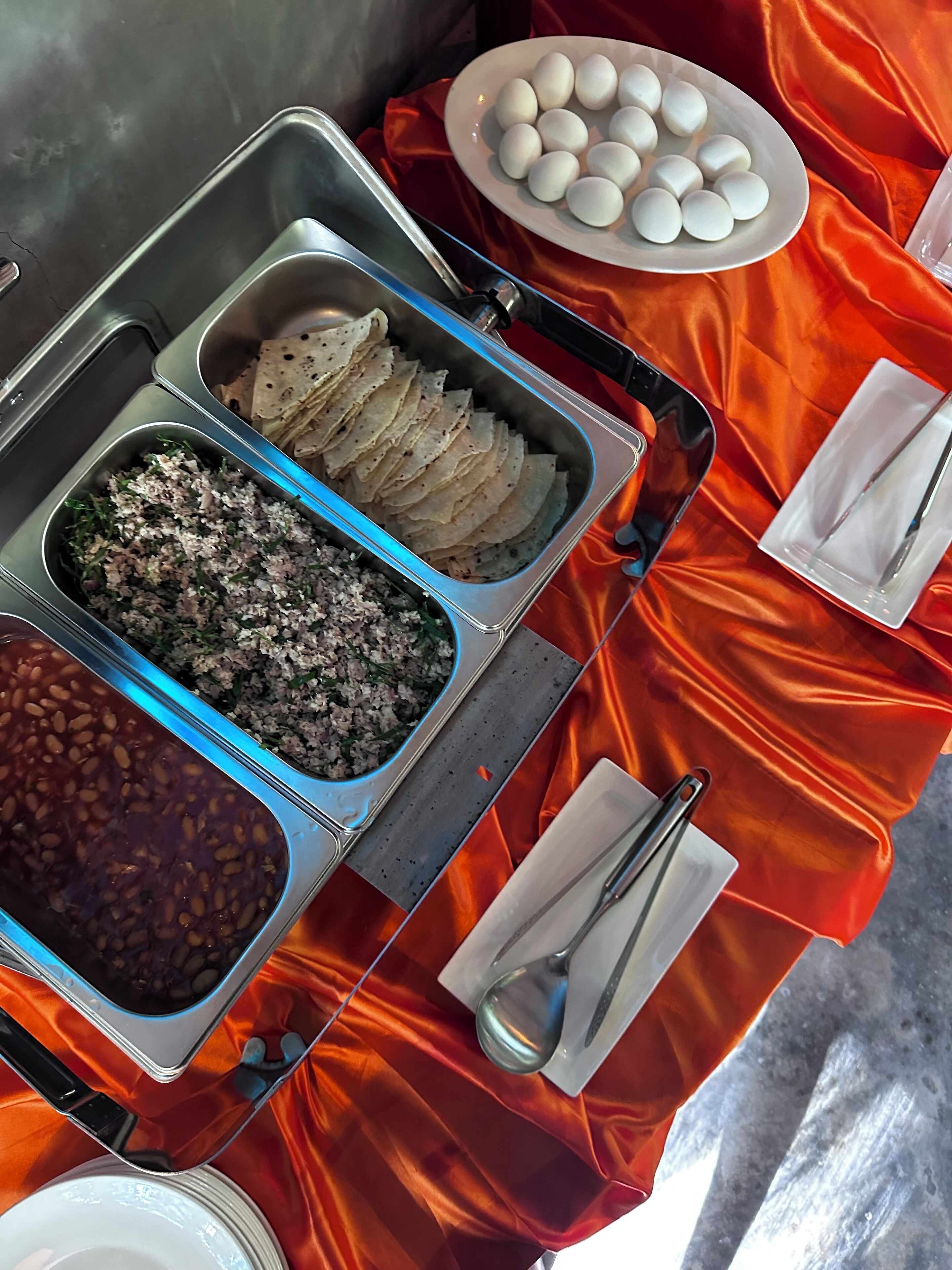 Disposição de buffet com diversos alimentos, incluindo feijão, carne e pães achatados em uma bandeja.