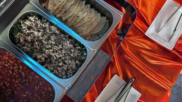 Disposição de buffet com diversos alimentos, incluindo feijão, carne e pães achatados em uma bandeja.