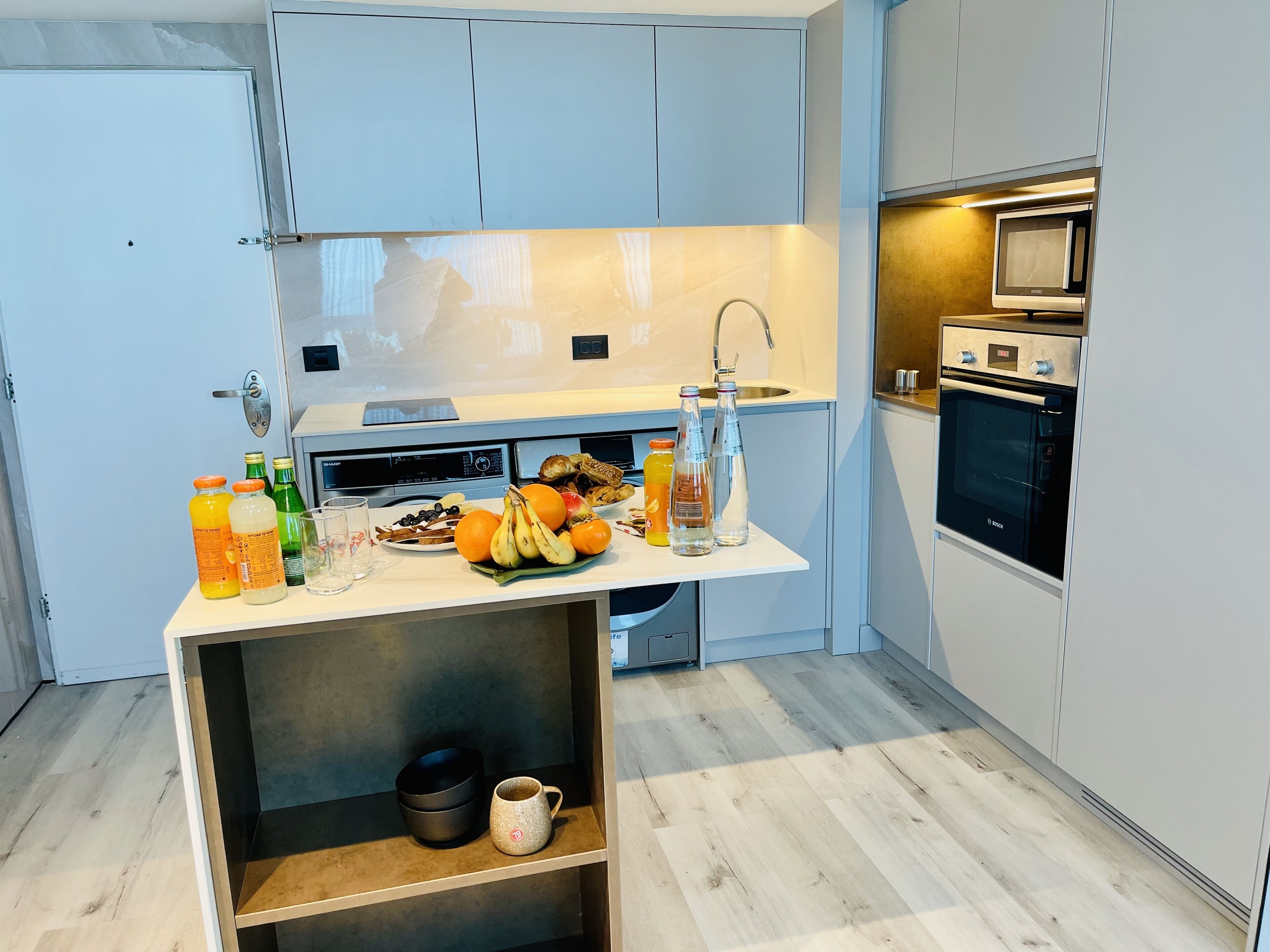 Uma cozinha moderna com bancada branca, pia e forno Bosch. Há diversos alimentos e bebidas sobre a bancada.