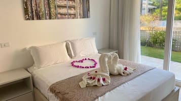 Cama bem arrumada com lençóis brancos e toalhas decorativas, um lei em formato de coração e uma obra de arte na parede acima.