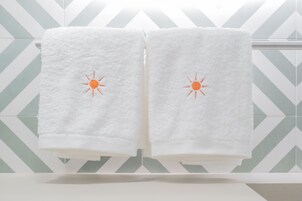 Duas toalhas brancas com desenhos de sol em laranja penduradas em um suporte.