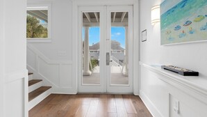Um corredor com paredes brancas, piso de madeira e porta de vidro que dá para o exterior.