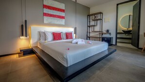 Quarto de hotel moderno com uma cama grande, mesas de cabeceira, abajur, obra de arte na parede, prateleira embutida e banheiro com pia e espelho.