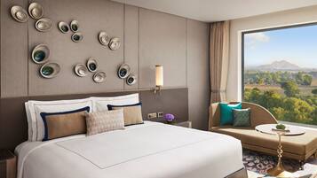 Quarto de hotel com uma cama grande, um sofá, vista para o exterior e arte decorativa nas paredes.