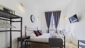 Um quarto com cama beliche, escrivaninha, cadeira, televisão, relógio e janela com cortinas.