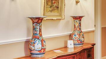 Um corredor com um armário de madeira, dois vasos ornamentados e luminárias fixadas na parede.