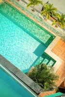 Piscina com água azul cristalina, rodeada por um deck ladrilhado e palmeiras.