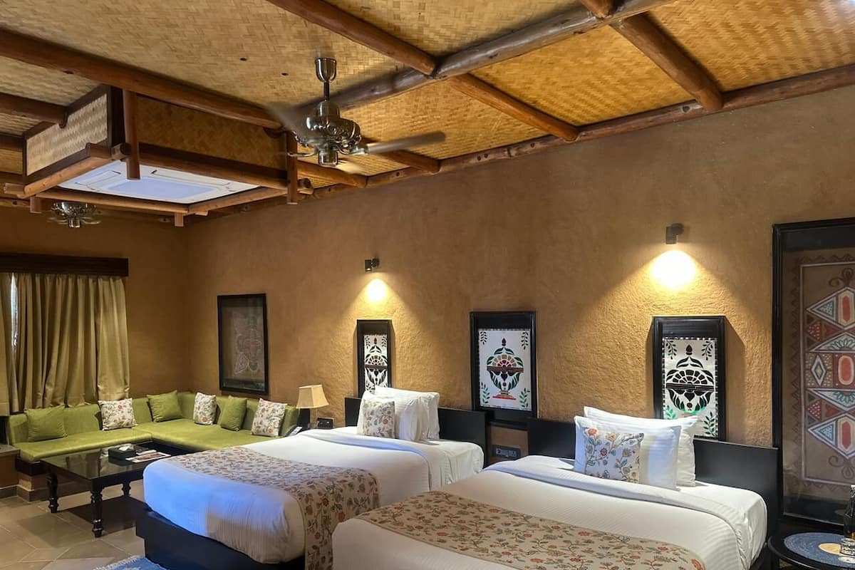 Quarto de hotel com duas camas, um sofá, uma mesa de centro e um ventilador de teto.