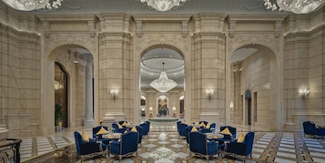 Um hall imponente com tetos altos, colunas ricamente decoradas e um lustre central.